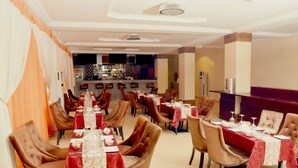 Restaurante com várias mesas preparadas para refeições, com toalhas de mesa vermelhas e brancas e cadeiras estofadas em castanho.