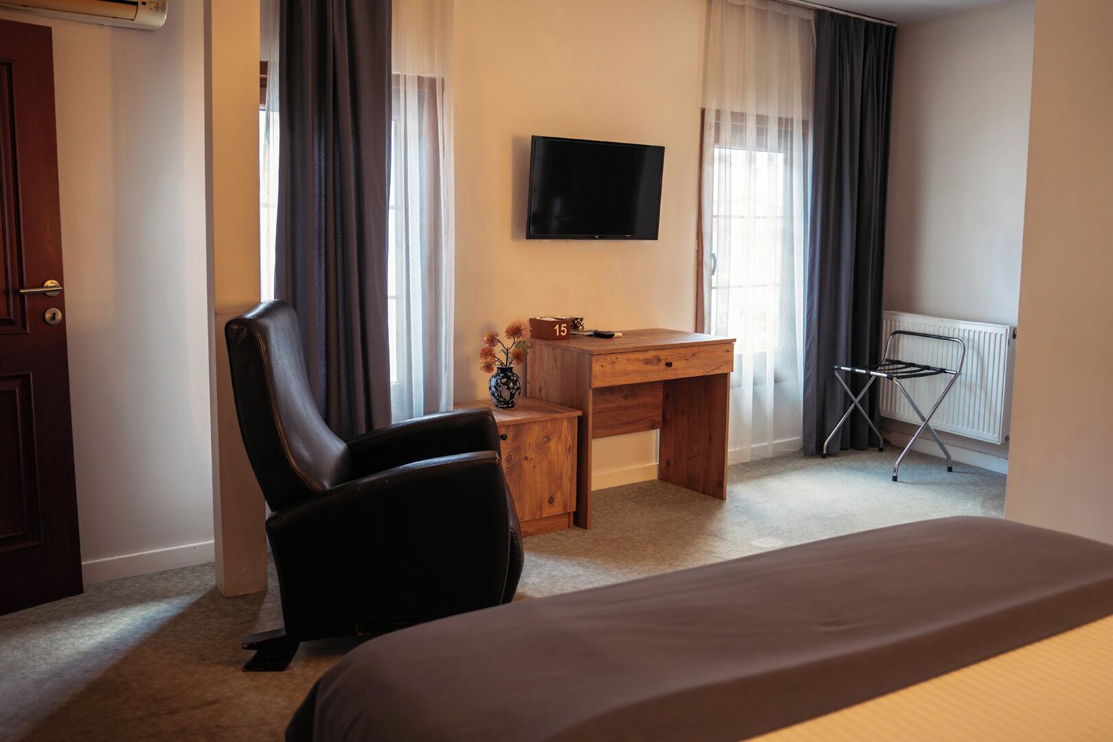 Quarto de hotel com cama, escrivaninha, cadeira, televisão e radiador.