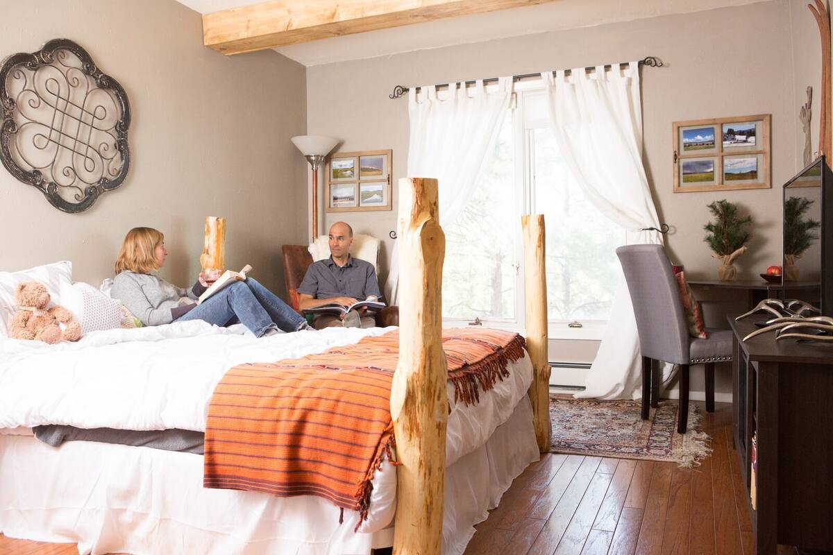 Um quarto com uma cama grande, uma cama de dossel de madeira, uma escrivaninha com cadeira e uma janela com cortinas.