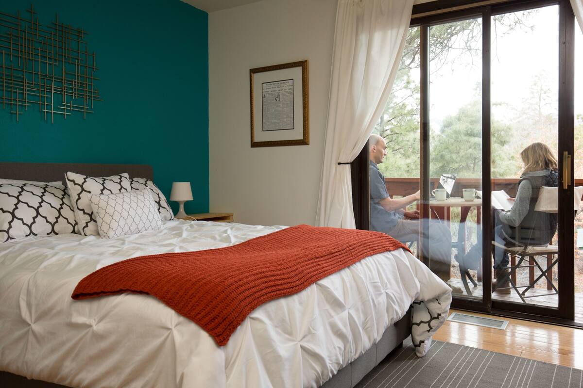 Quarto com uma cama grande, uma parede em tom de verde-água, um certificado emoldurado e vista para um deck externo.