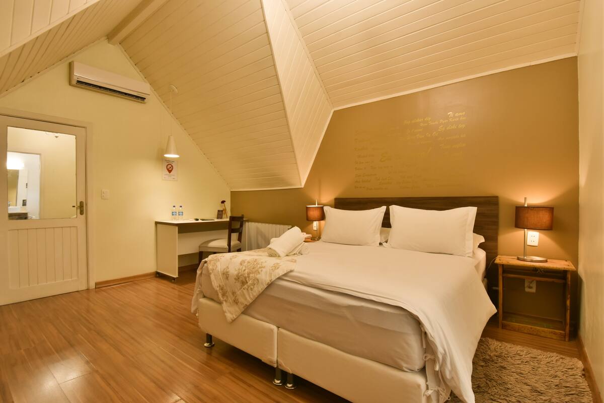 Quarto com uma cama grande, mesas de cabeceira, escrivaninha e uma cadeira.