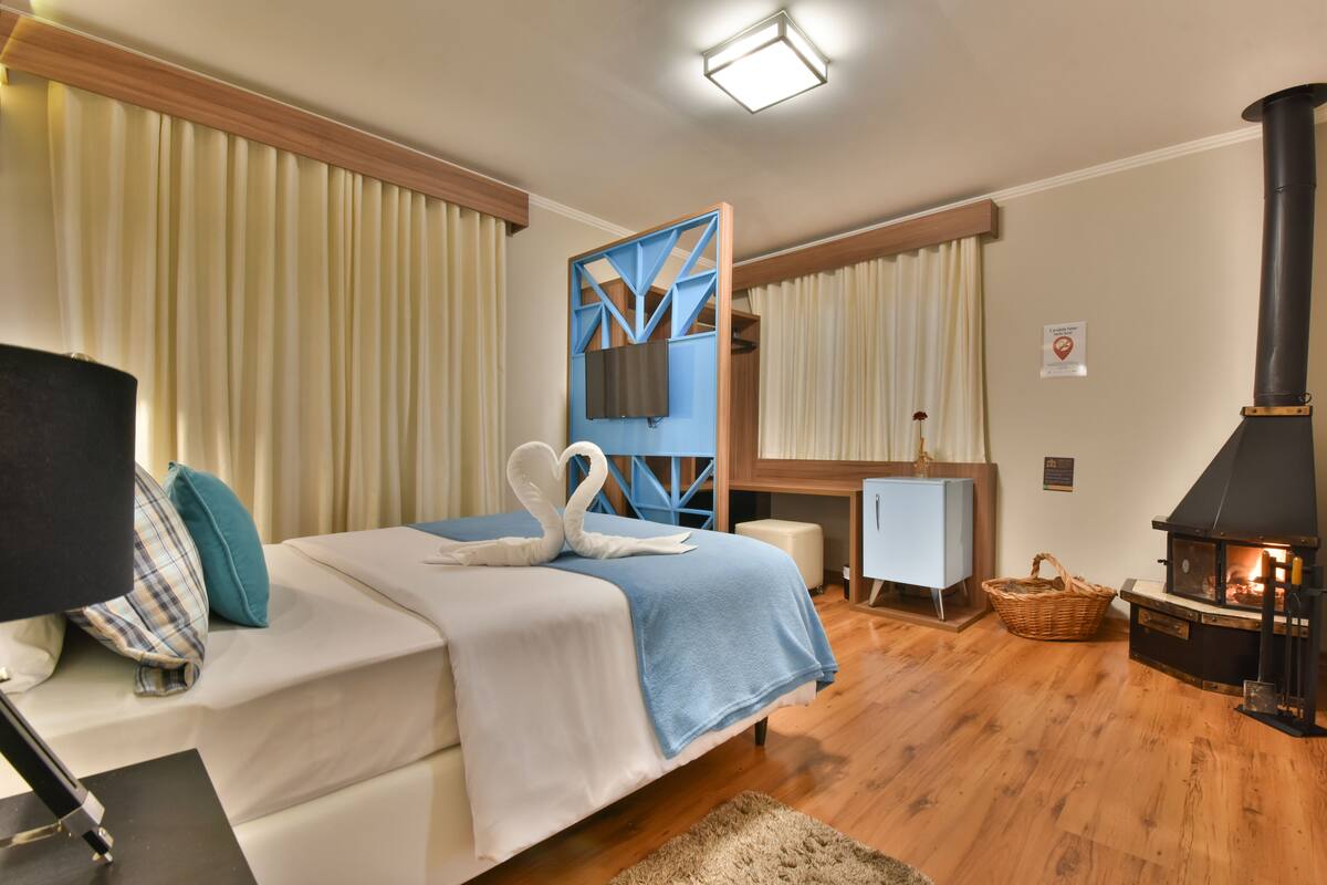 Quarto de hotel com cama, lareira, televisão e piso de madeira.