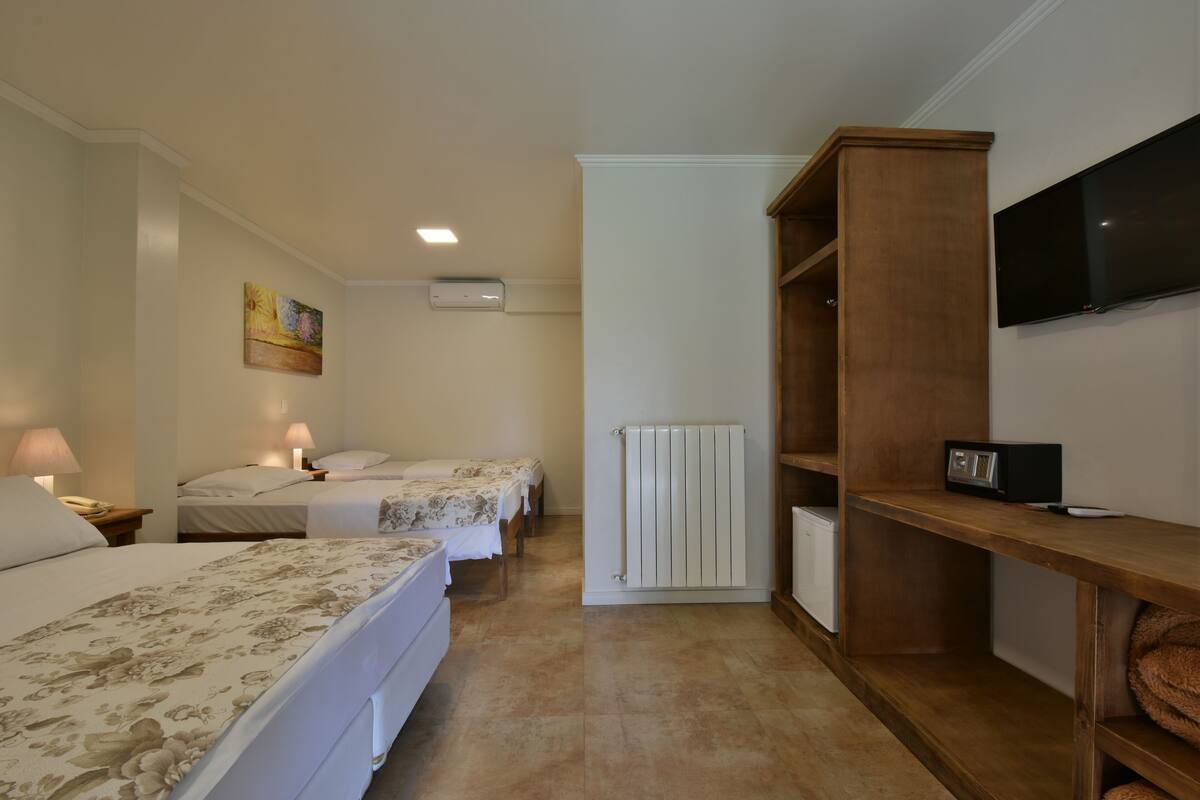 Quarto de hotel com duas camas de solteiro, um móvel de madeira para televisão, um radiador e um pequeno armário branco.