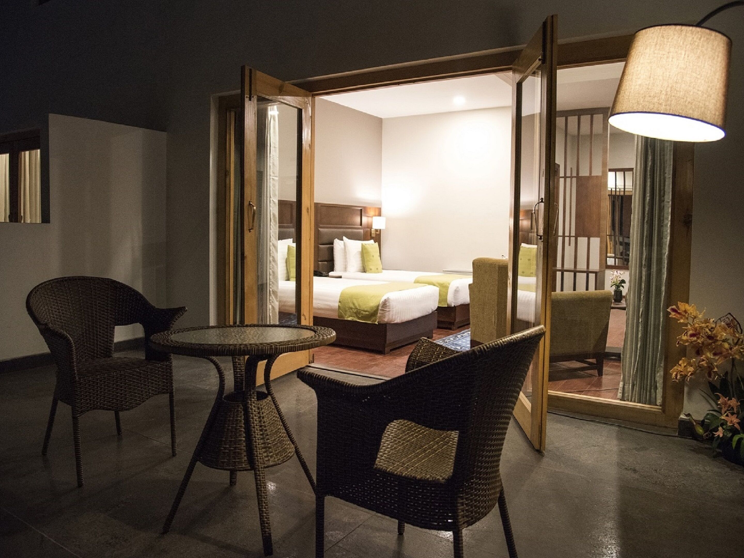 Quarto de hotel com cama, uma mesinha, duas cadeiras e uma janela grande.