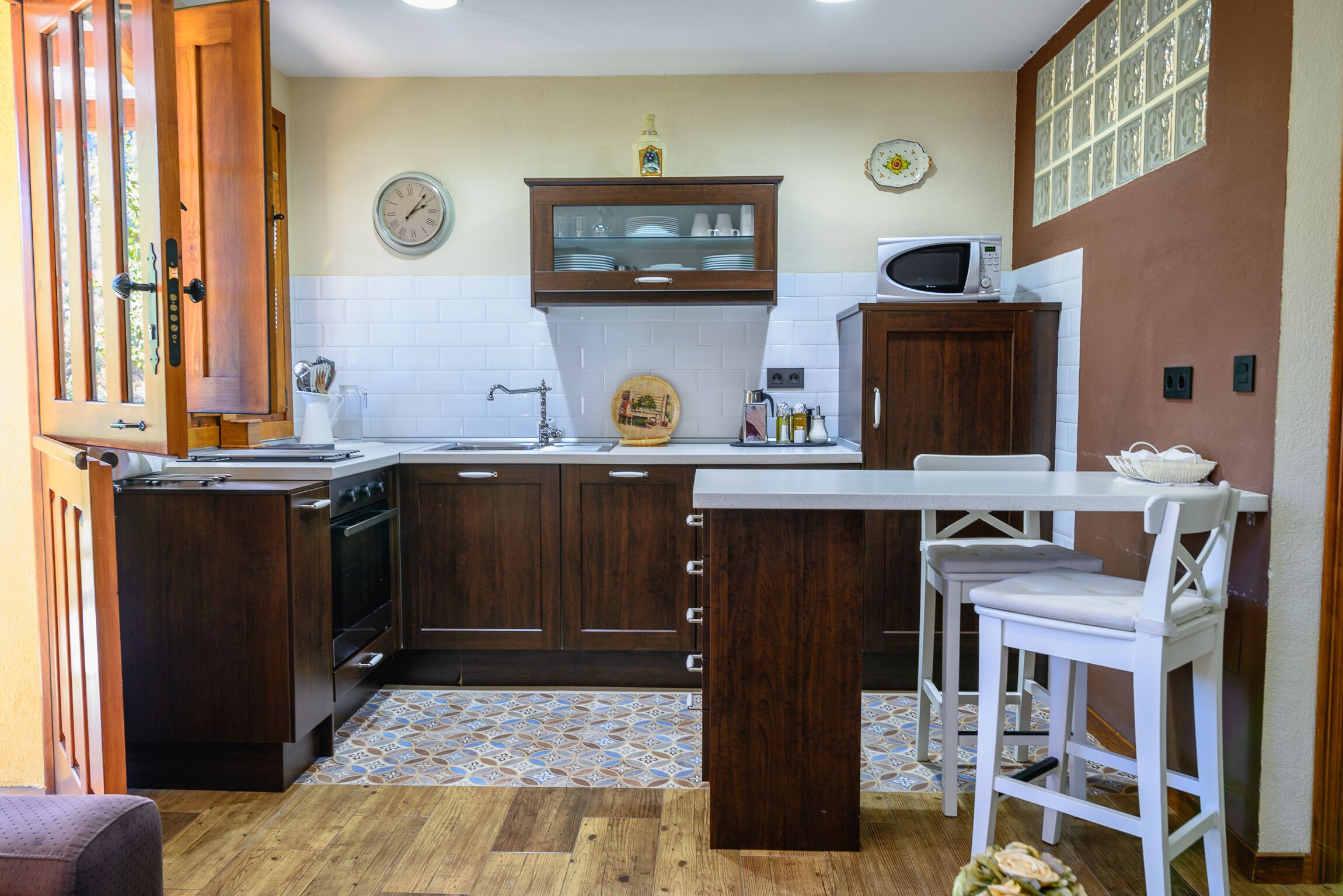 Uma cozinha com armários de madeira, um micro-ondas e um espaço de refeições com uma mesa e cadeiras brancas.