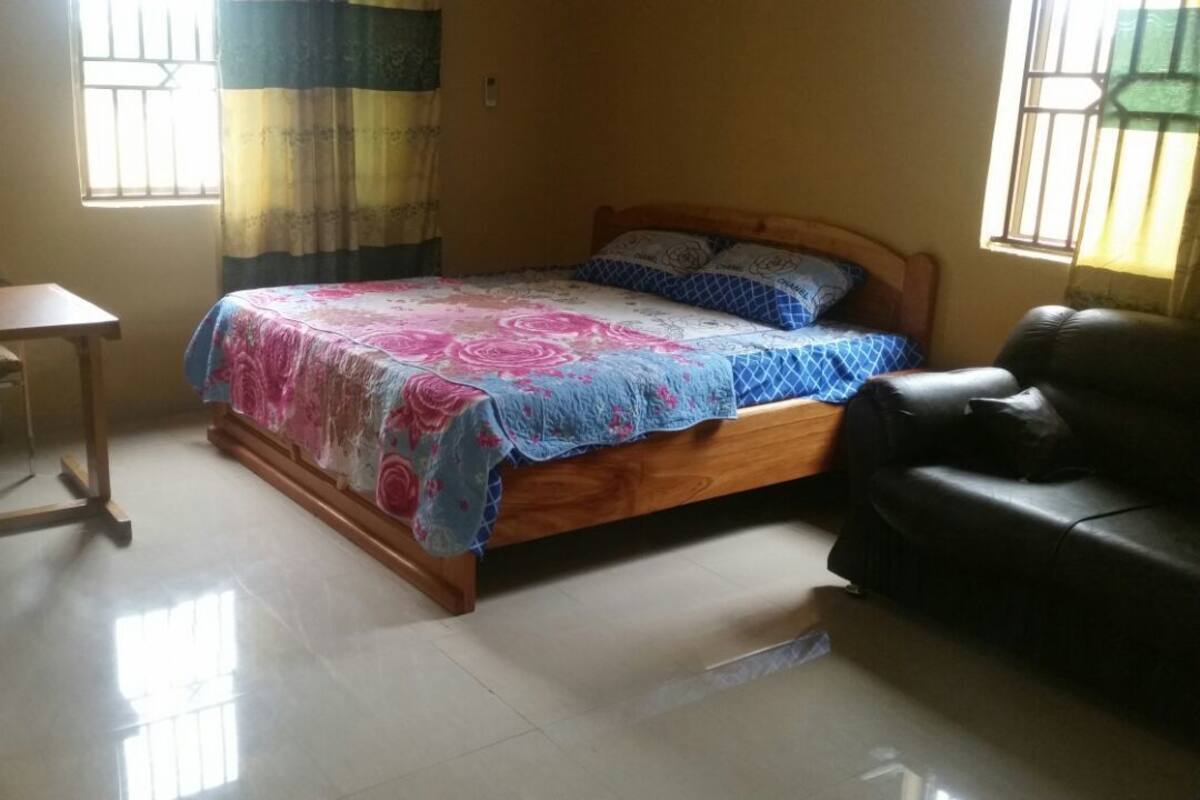 Quarto com cama de madeira, uma mesinha e uma poltrona de couro.