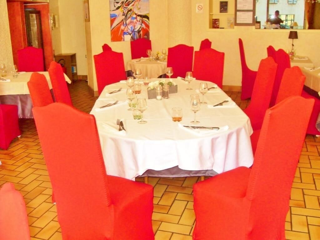 Uma área de refeições com mesas redondas, cadeiras vermelhas e toalhas de mesa brancas.
