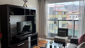 Uma sala de estar moderna com televisão de tela plana, móvel de entretenimento escuro, mesa de centro de vidro e um sofá.