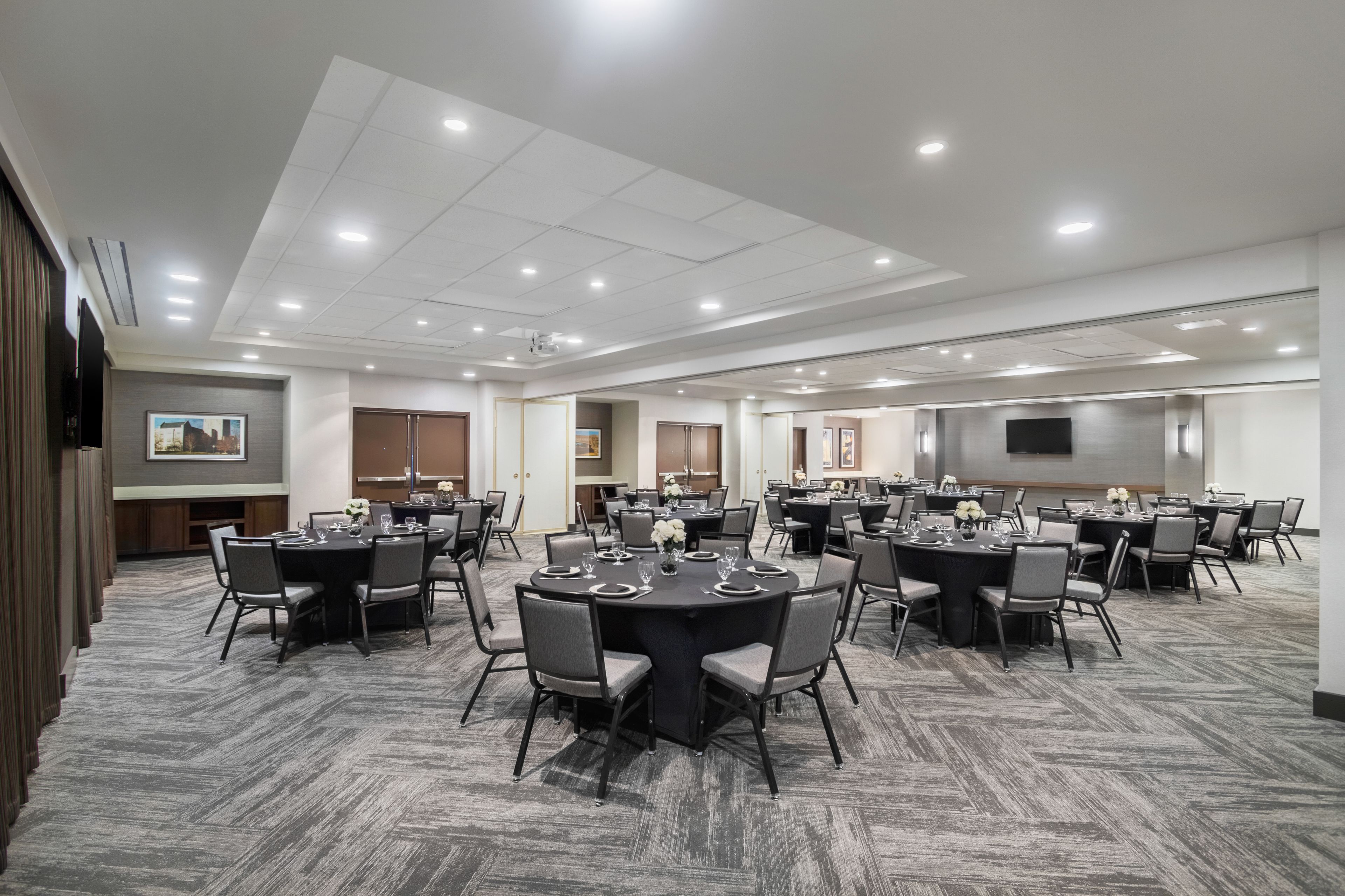 Sala de conferência com várias mesas e cadeiras, equipada com placas de identificação e centros de mesa florais.