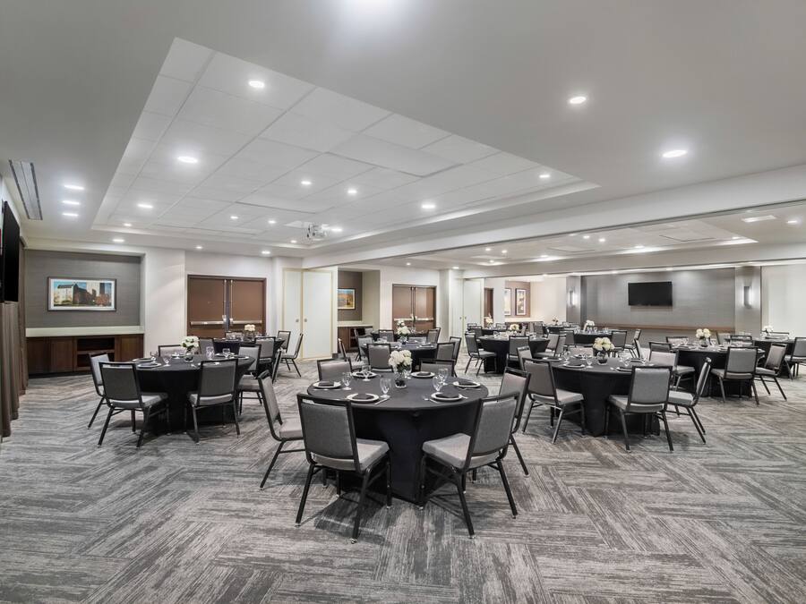 Sala de conferência com várias mesas e cadeiras, equipada com placas de identificação e centros de mesa florais.