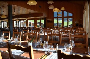 Restaurante com interiores em madeira, grandes janelas e mesas preparadas para refeições.