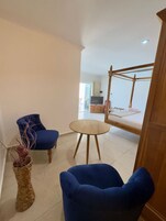 Quarto com cama, duas poltronas azuis, uma mesinha redonda e uma rede de madeira.