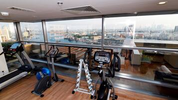 Uma academia com equipamento de exercícios e uma grande janela com vista para a paisagem urbana.