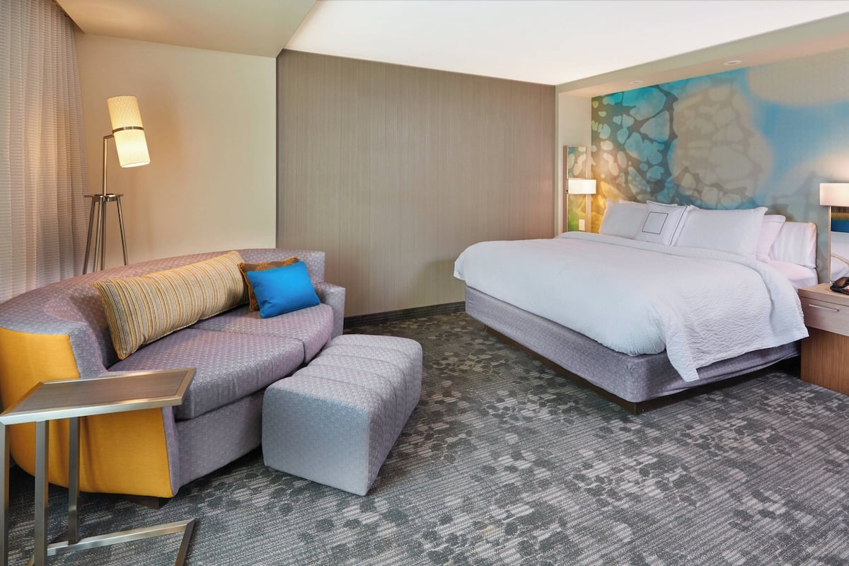 Quarto de hotel com cama, sofá, pequena mesa e luminária.