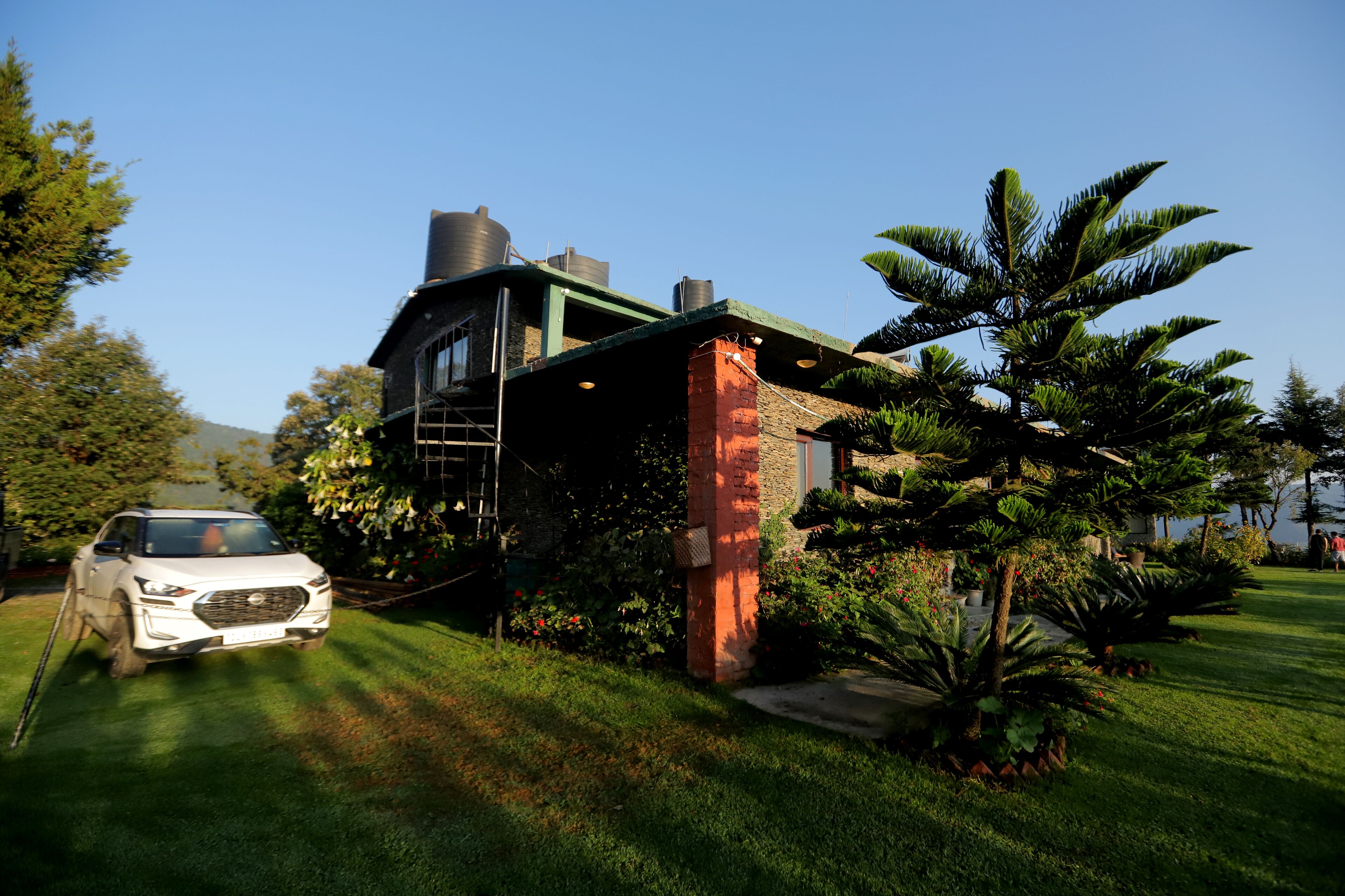 Uma casa com garagem, um pilar de tijolos e um gramado com diversas plantas.