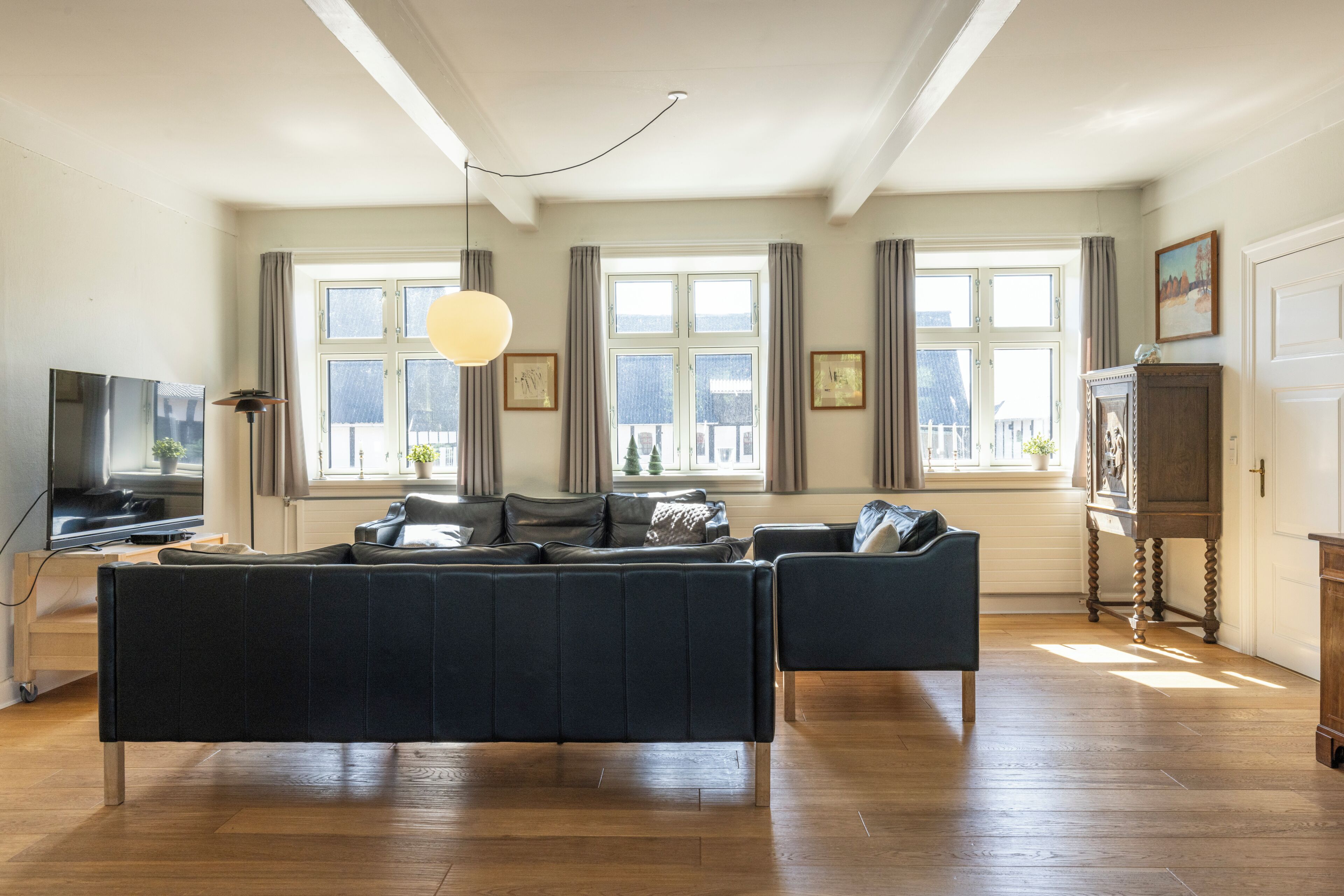Uma sala de estar ampla com um sofá preto grande, uma televisão e um armário de madeira.
