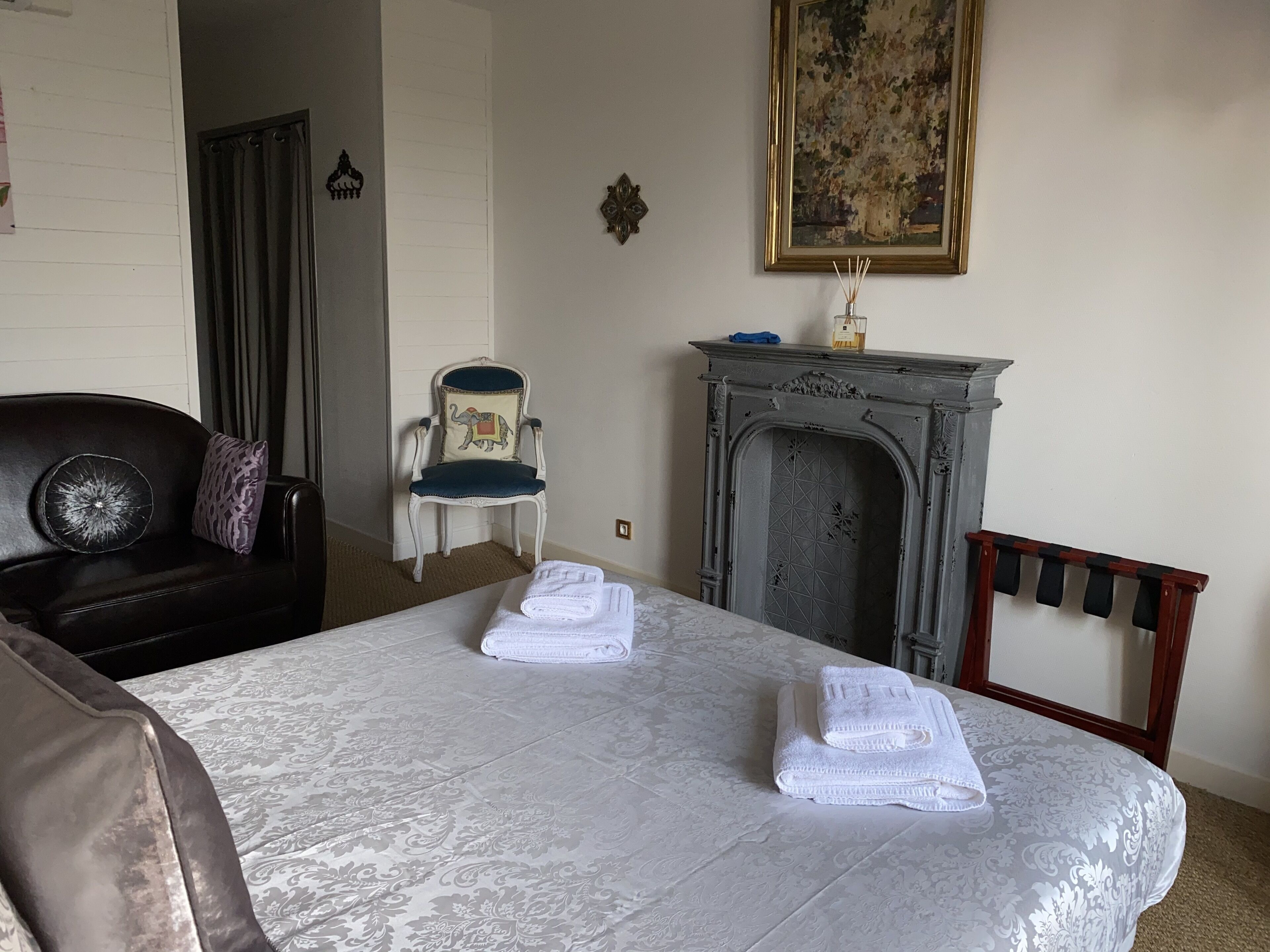 Quarto de hotel com cama, uma cadeira, lareira e um quadro na parede.