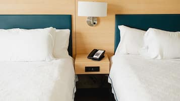 Quarto de hotel com duas camas, uma mesa de cabeceira com abajur e uma gaveta pequena.
