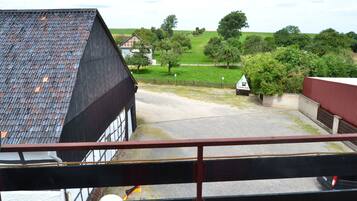 Vista de uma varanda com vista para zona rural, com um edifício de telhado inclinado, área cercada e uma estrada com sinal de trânsito.