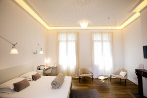 Quarto de hotel com cama, duas cadeiras, escrivaninha e lareira.