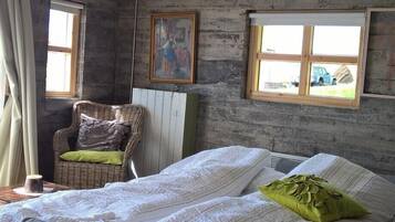 Quarto com cama, uma cadeira de vime, um quadro e uma janela com vista.