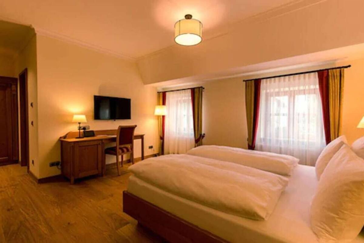 Quarto de hotel com cama grande, escrivaninha com cadeira, televisão de tela plana e janela com cortinas.