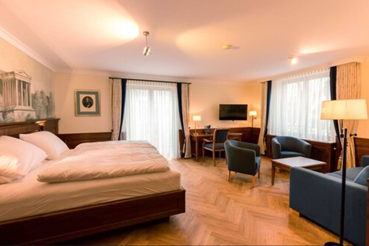 Quarto de hotel com uma cama grande, uma escrivaninha, uma cadeira, um sofá e uma televisão.