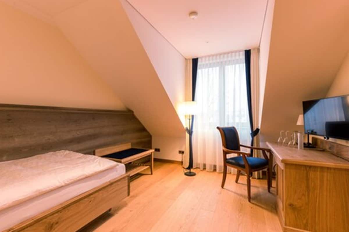 Quarto de hotel pequeno e moderno, com cama mezanina, escrivaninha, cadeira e televisão.