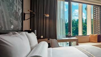 Quarto de hotel moderno com uma cama grande, uma escrivaninha e vista para a cidade através de amplas janelas.