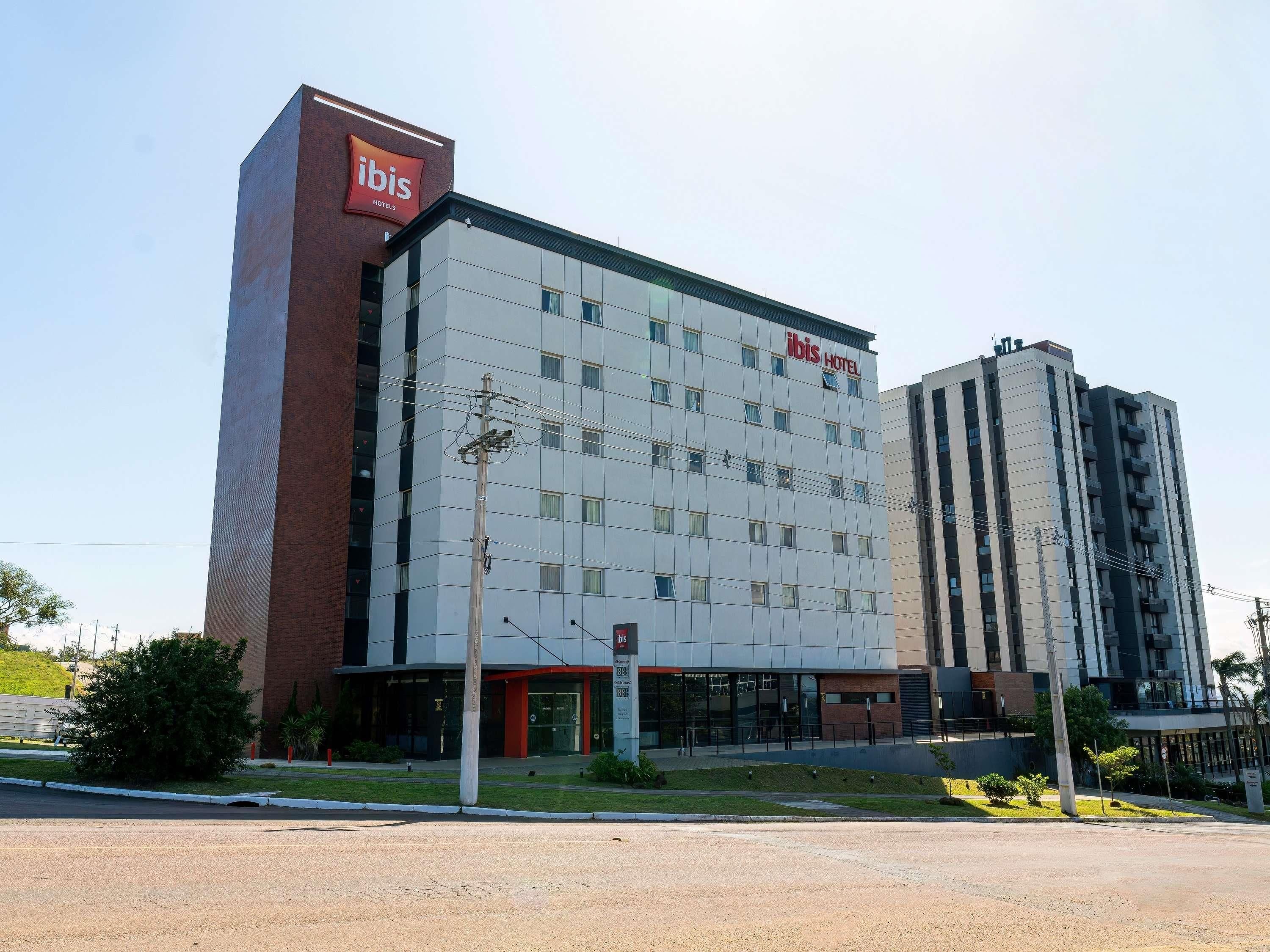 Um edifício moderno de hotel com um destaque para a placa 'ibis', vários andares e fachada plana.