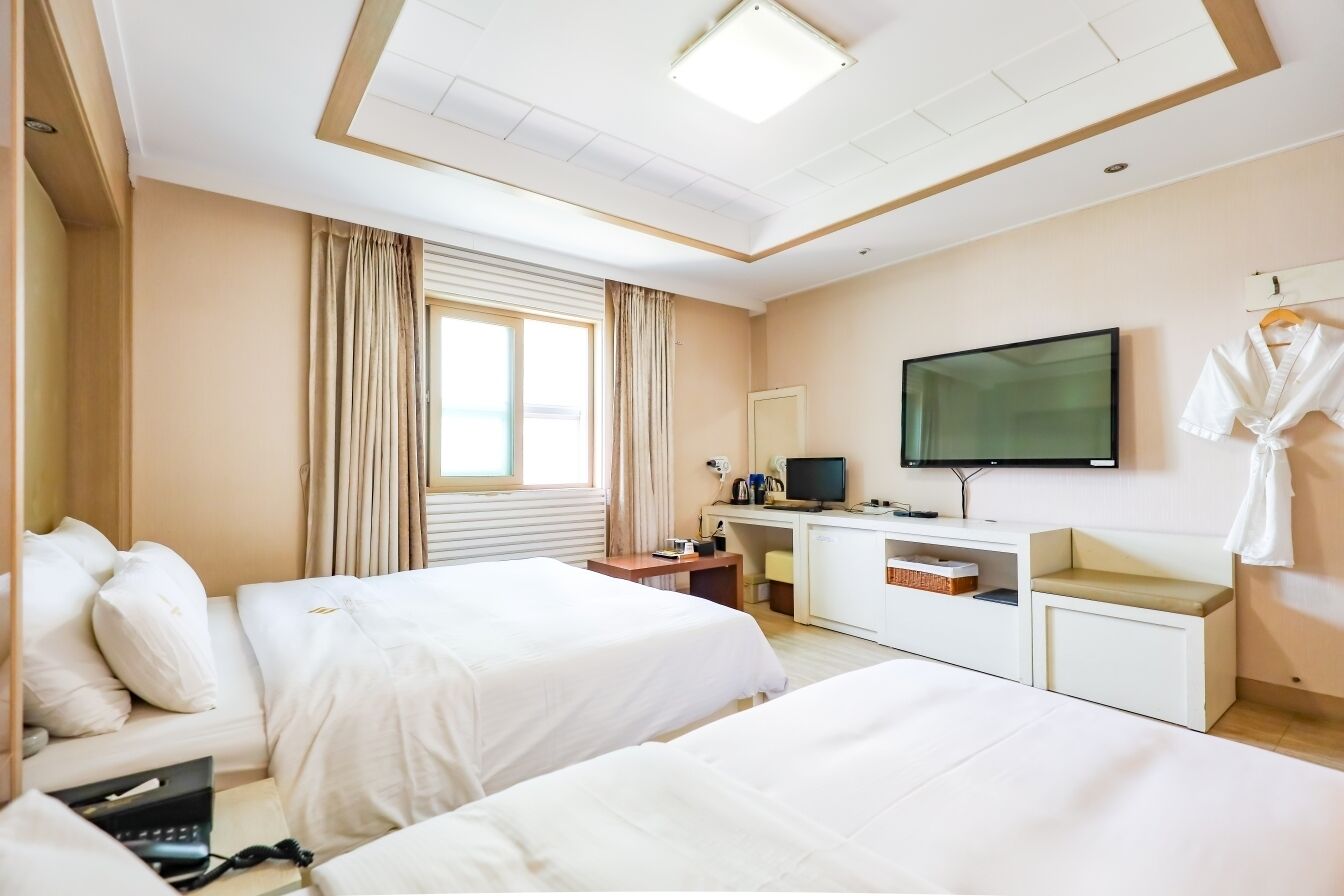 Quarto de hotel com duas camas, uma secretária com televisão e um roupão pendurado na parede.