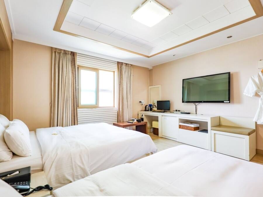 Quarto de hotel com duas camas, uma secretária com televisão e um roupão pendurado na parede.