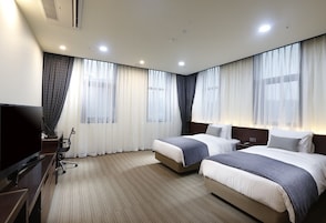 Quarto de hotel com duas camas, televisão, escrivaninha e uma cadeira.