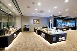 Um saguão de hotel moderno com área de buffet, balcão de recepção e cozinha visível ao fundo.