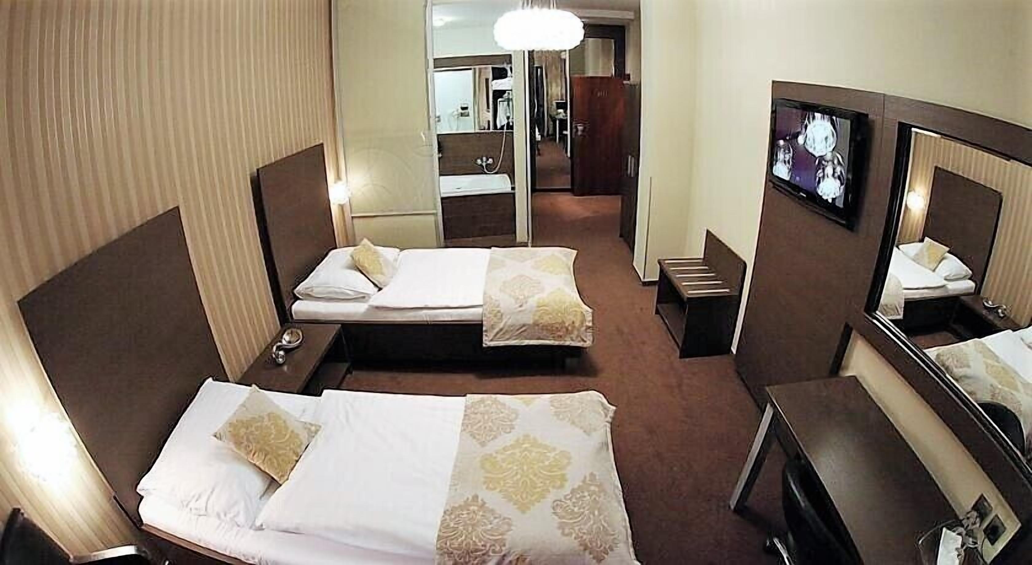 Quarto de hotel com duas camas, televisão, escrivaninha e espelho.
