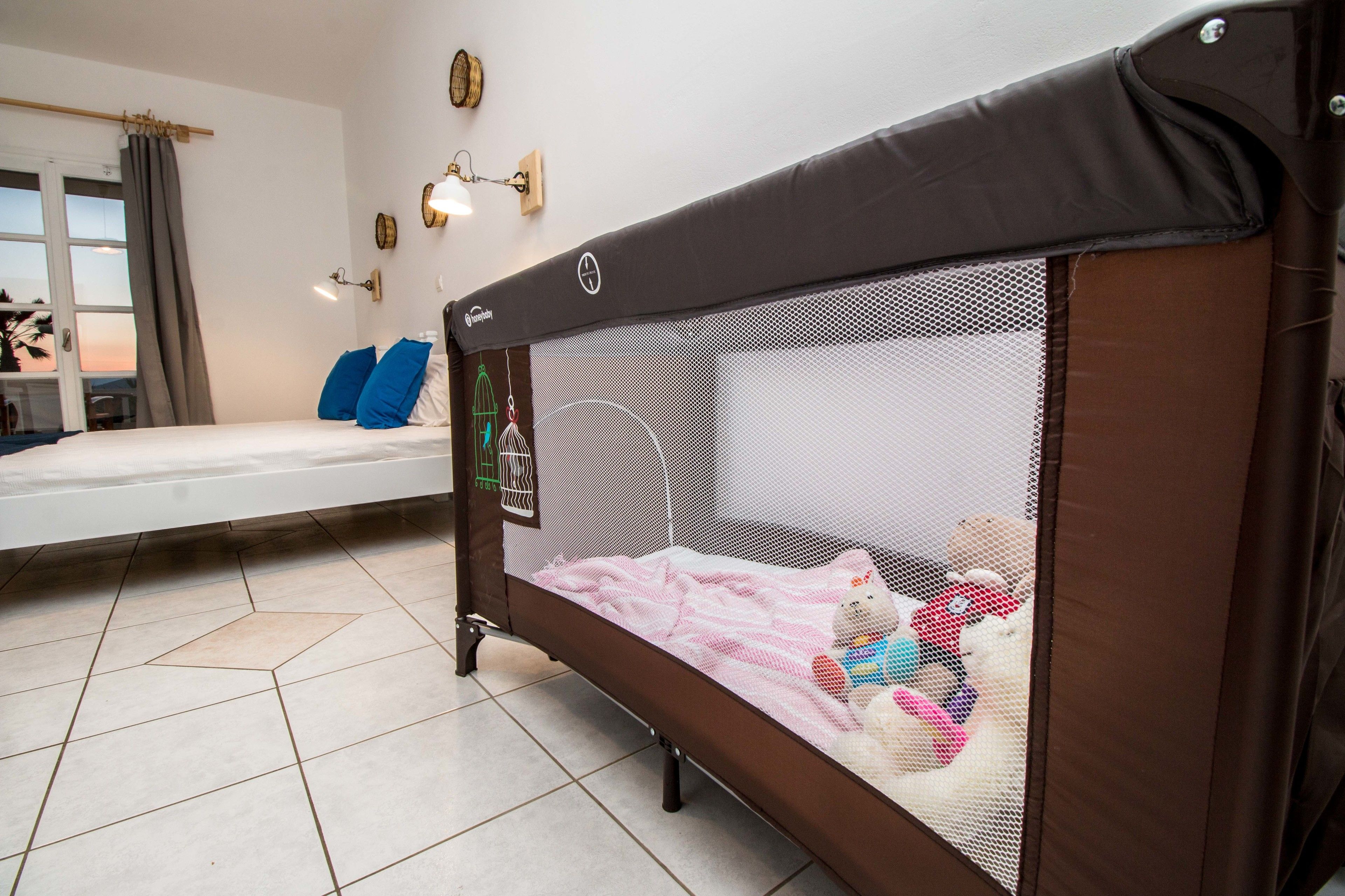 Quarto com cama, janela com cortinas, luminária na parede e uma pequena mesa com uma planta.