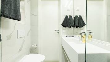 Um banheiro com vaso sanitário branco, pia com espelho e porta-toalhas com duas toalhas.