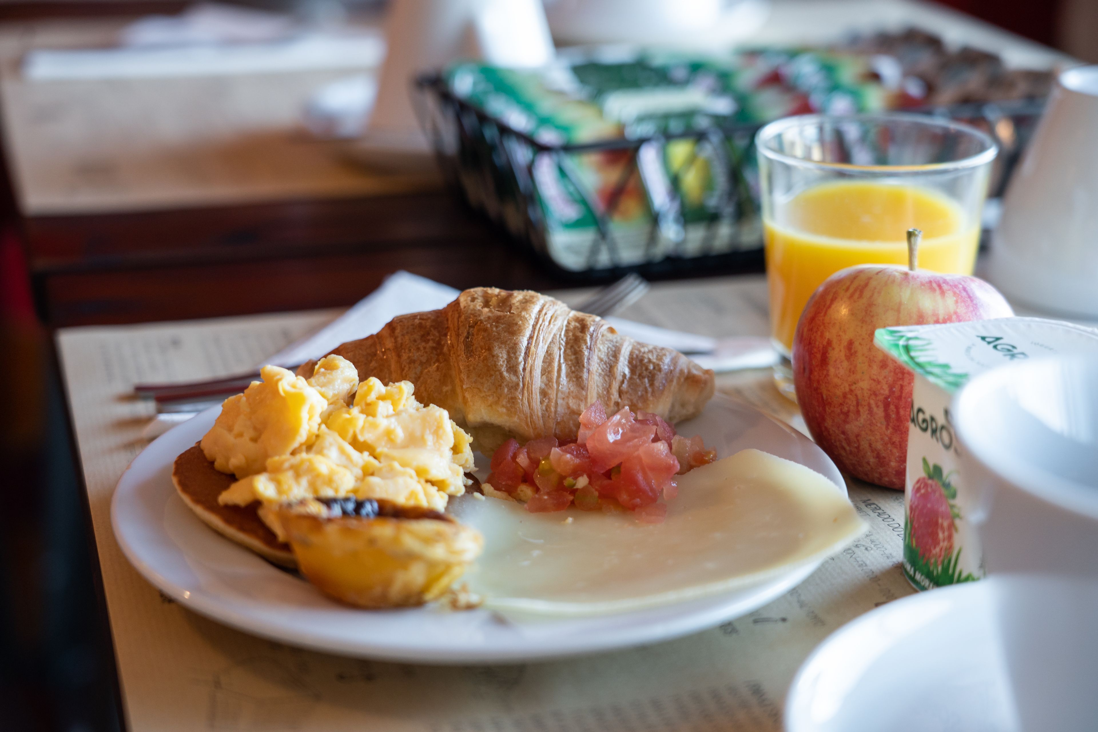 Prato de café da manhã com ovos mexidos, um croissant e molho de tomate.
