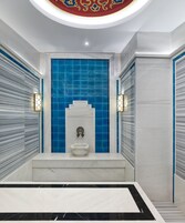 Um banheiro moderno com parede revestida em azulejos azuis, pia branca e duas luminárias na parede.