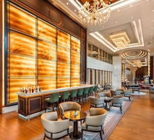 Um saguão de hotel moderno com área de bar, assentos e um lustre imponente.