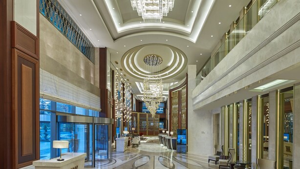 Um hall amplo com piso de mármore curvo no centro, um balcão de recepção e um lustre.
