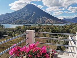Varanda com grades de metal vista para uma paisagem montanhosa e um lago.