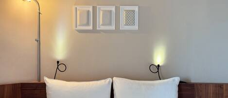 Cama bem arrumada com duas almofadas e cabeceira de madeira. Há três quadros na parede acima da cama.