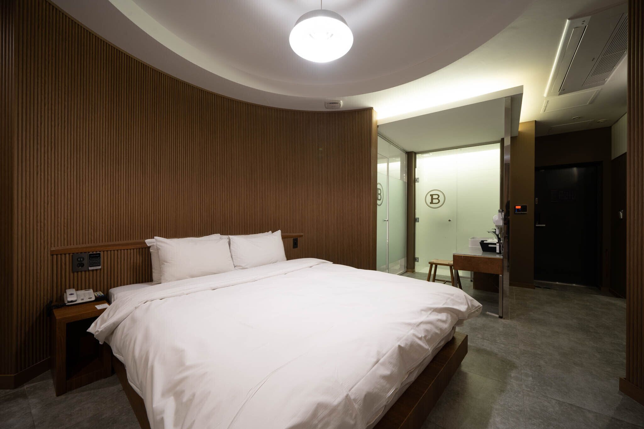 Quarto de hotel moderno com uma cama grande, uma mesinha de cabeceira com telefone e uma pequena escrivaninha com cadeira.