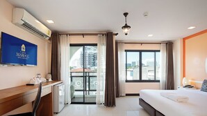 Quarto de hotel com uma cama, escrivaninha, televisão e varanda com cortinas.