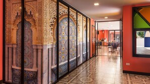 Um corredor com trabalhos em azulejos detalhados e vista para uma sala de jantar com mesas e cadeiras.