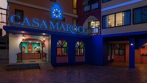 Exterior do Casa Maroc Hotel & Resort, com uma placa iluminada em destaque, área de recepção e um pátio com piso estampado.