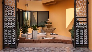 Uma entrada em arco com piso de azulejos, um portão de metal decorativo e uma fonte no pátio.