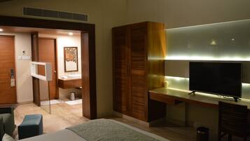 Quarto de hotel com cama, escrivaninha com televisão, espelho e guarda-roupa de madeira.
