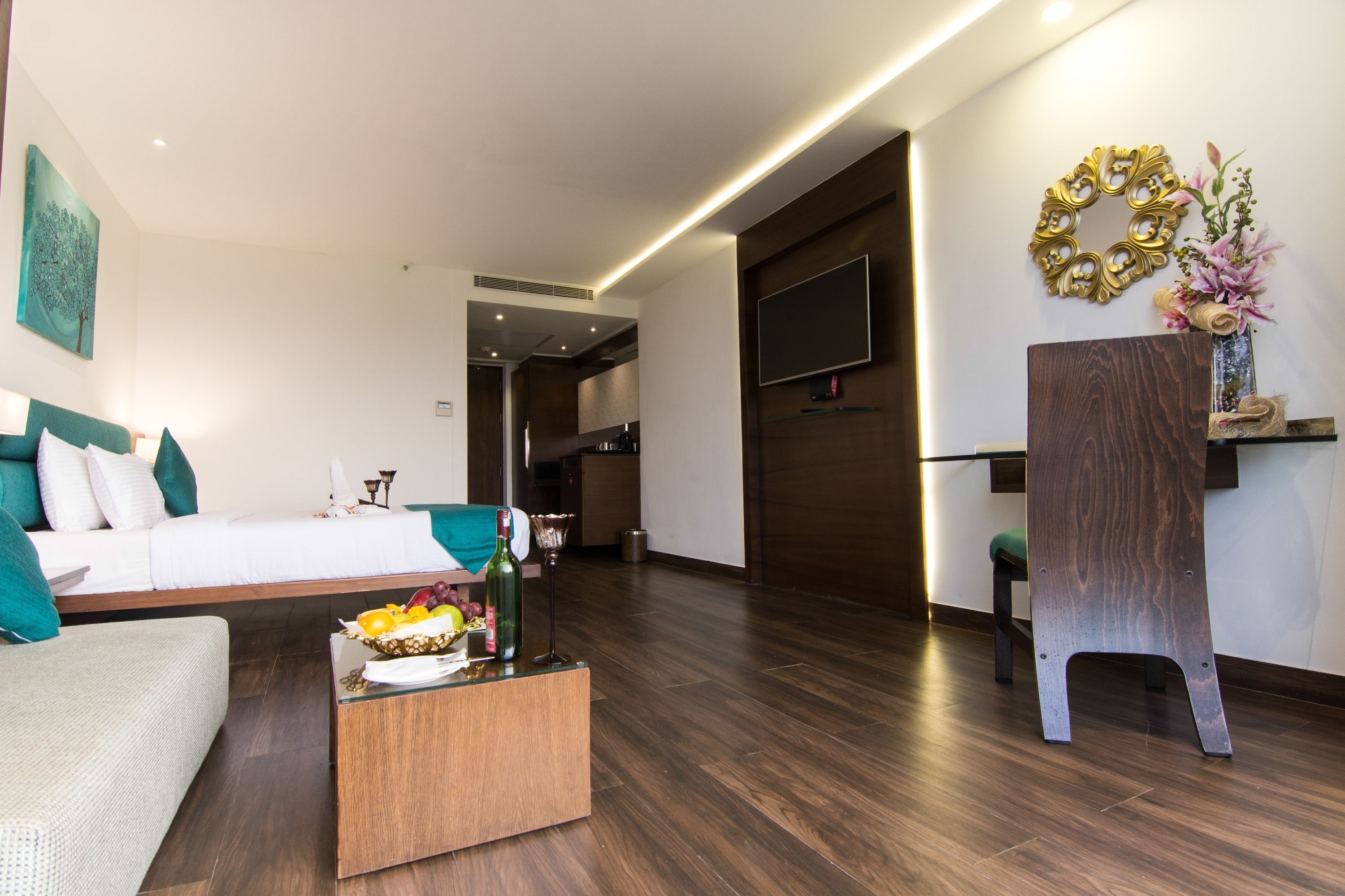 Quarto de hotel moderno com uma cama, área de estar com mesa de centro, televisão e painel decorativo de madeira.